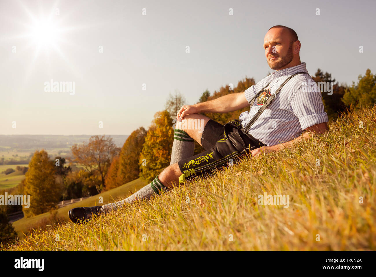 traditional clothed Bavarian man lying on an alpine pasture and looking ...