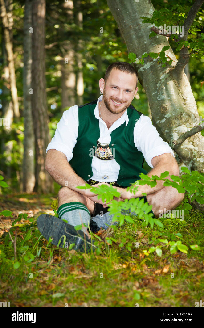 traditional clothed Bavarian man sitting in a forest at a tree, Germany ...