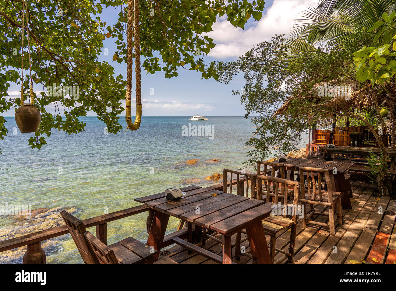 Wooden table and chairs in empty beach cafe next to sea water. Close up. Island Koh Phangan ...