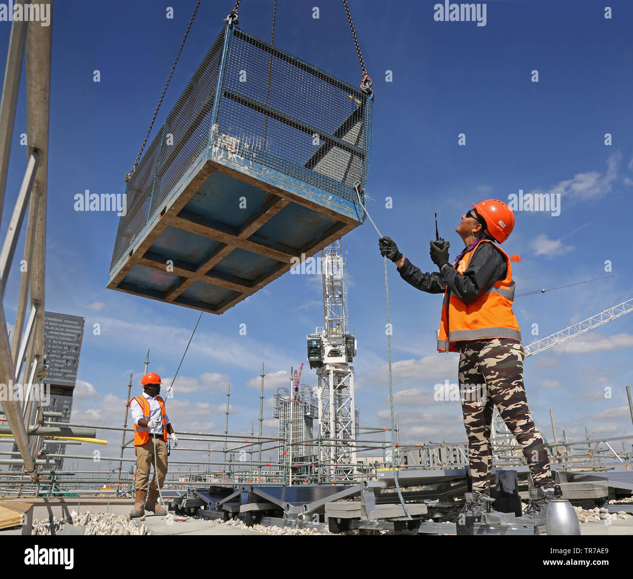 A female construction worker guides an access platform as it is lowered ...