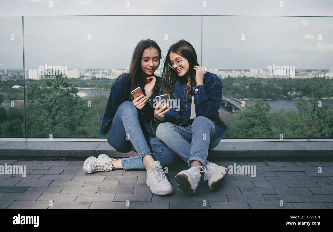 Two happy young best friends using social media on their smartphon ...