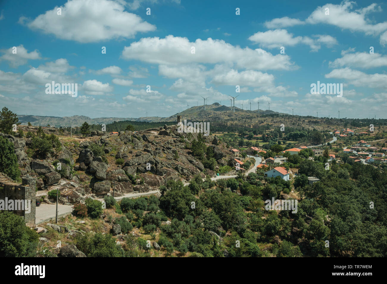 Hilly landscape with rocks and wind turbines on top and few rooftops at ...