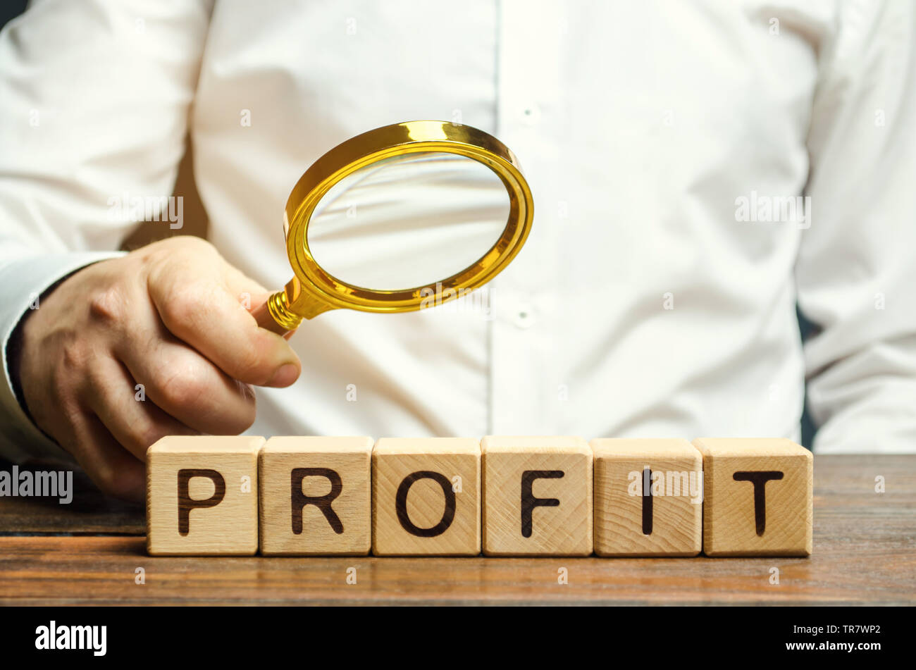 Businessman holds a magnifying glass over the word Profit. The concept ...