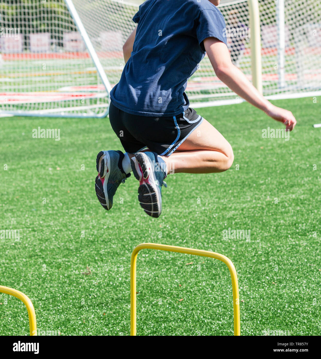A high school runner is cross training by jumping over tow foot high yellow mini hurdles on a ...