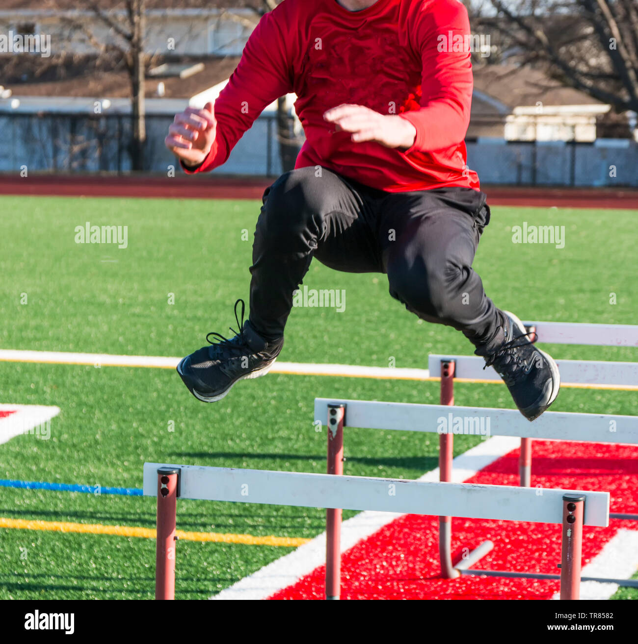 A high school runner is bounding over hurdles on a turf field during ...