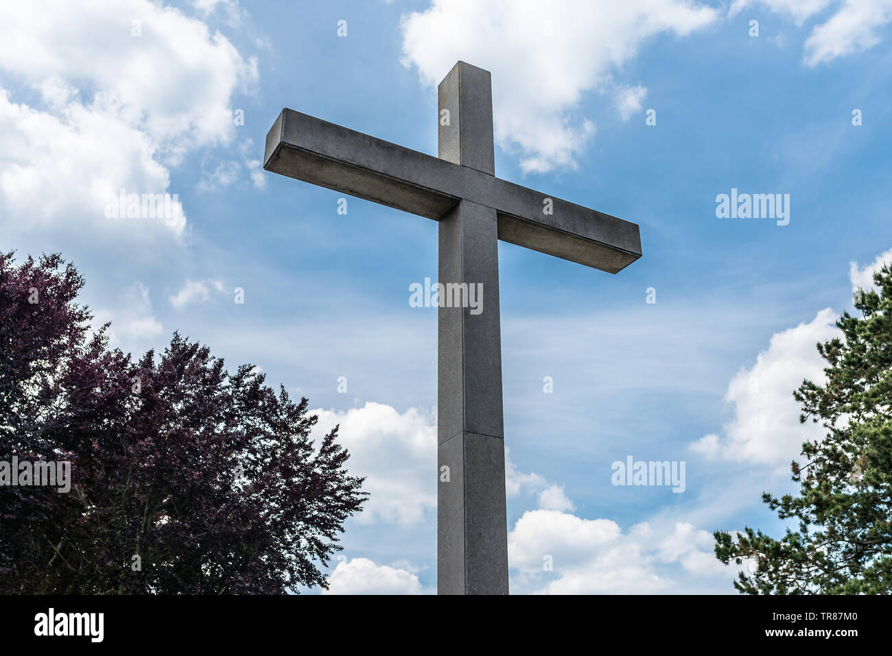 A large concrete cross on a cemetery against a blue sky with white ...
