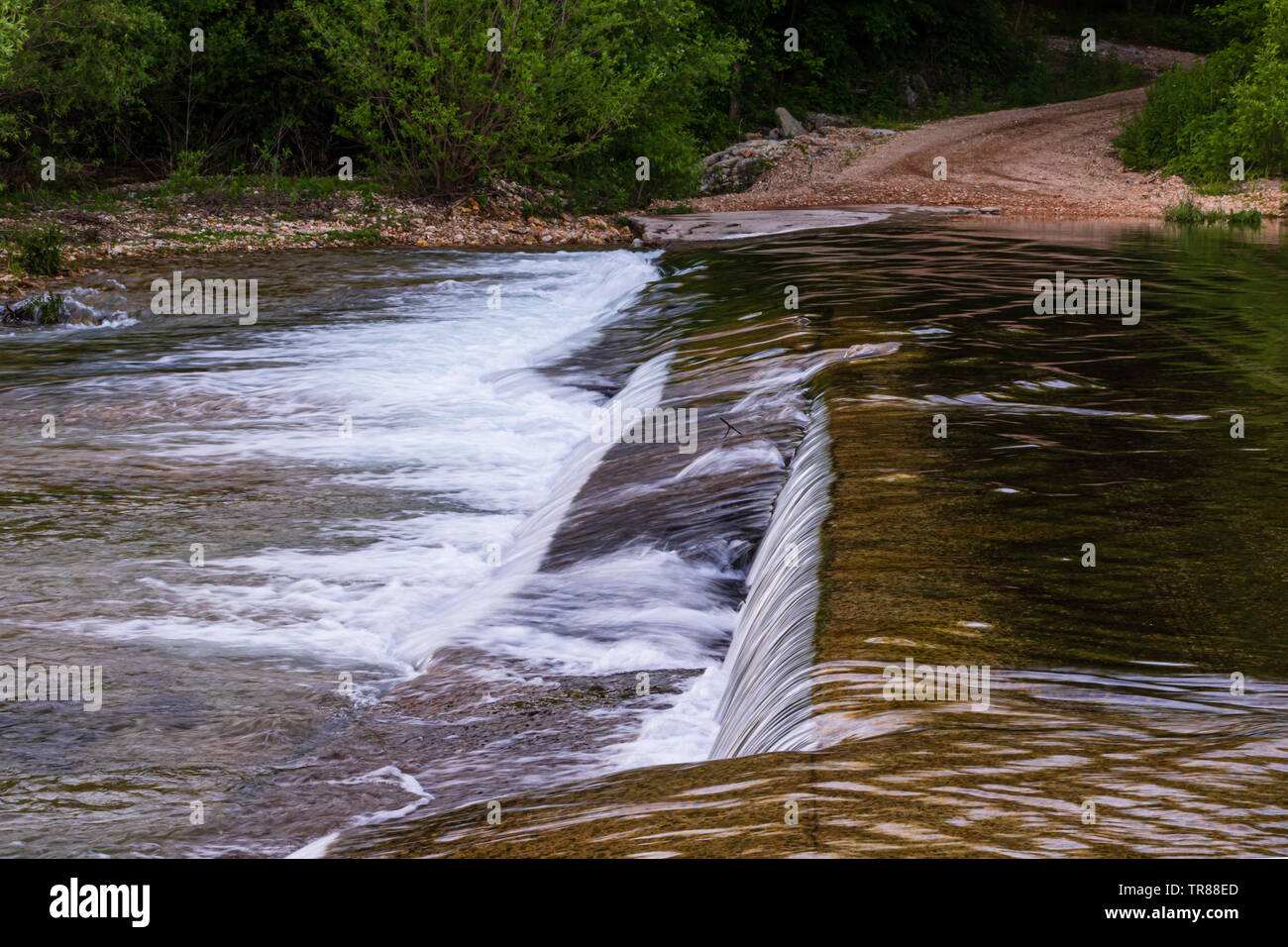 The water of Spring Creek flowing over the concrete slab bridge located ...