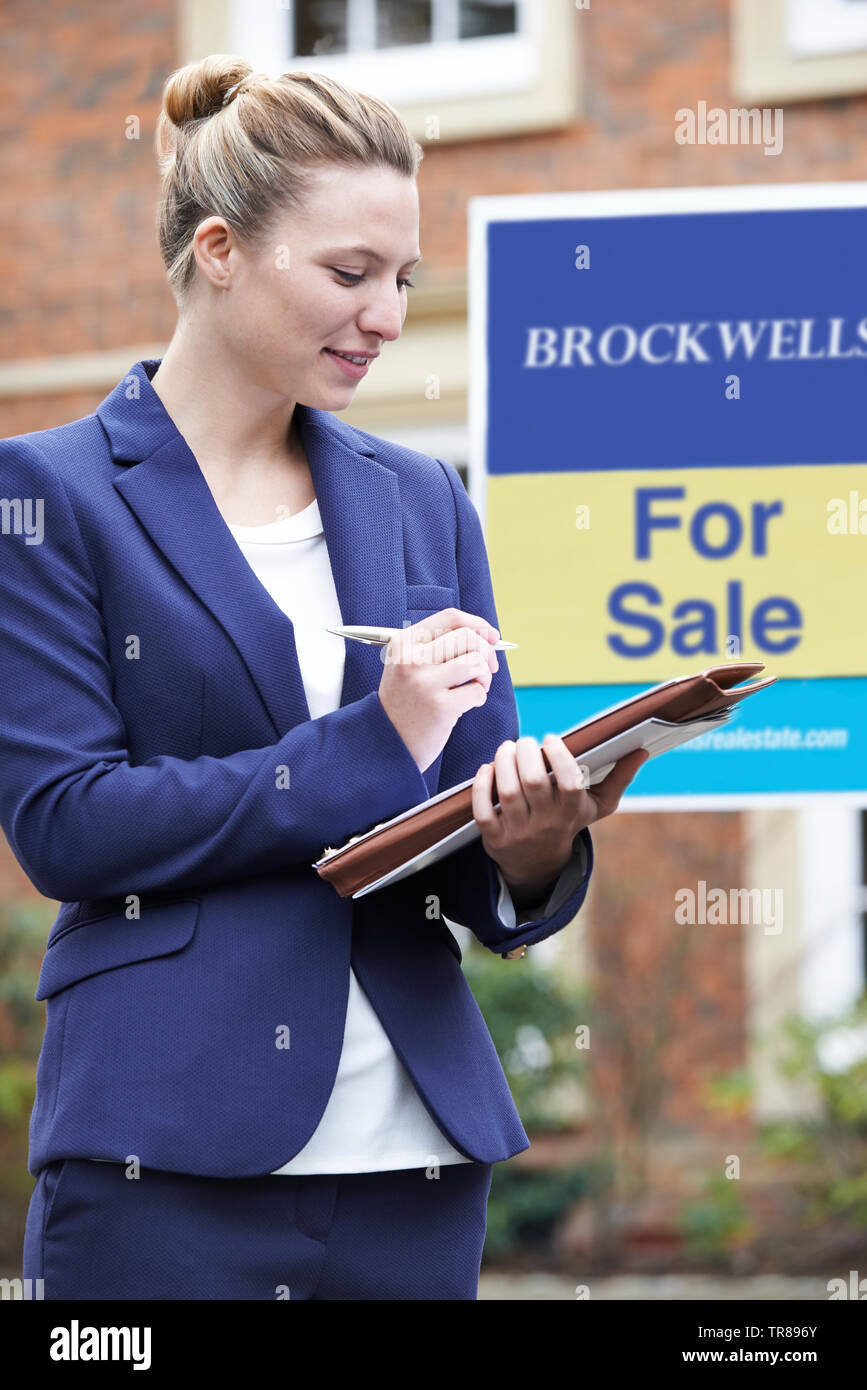 Female Realtor Standing Making Notes Outside Residential Property With ...