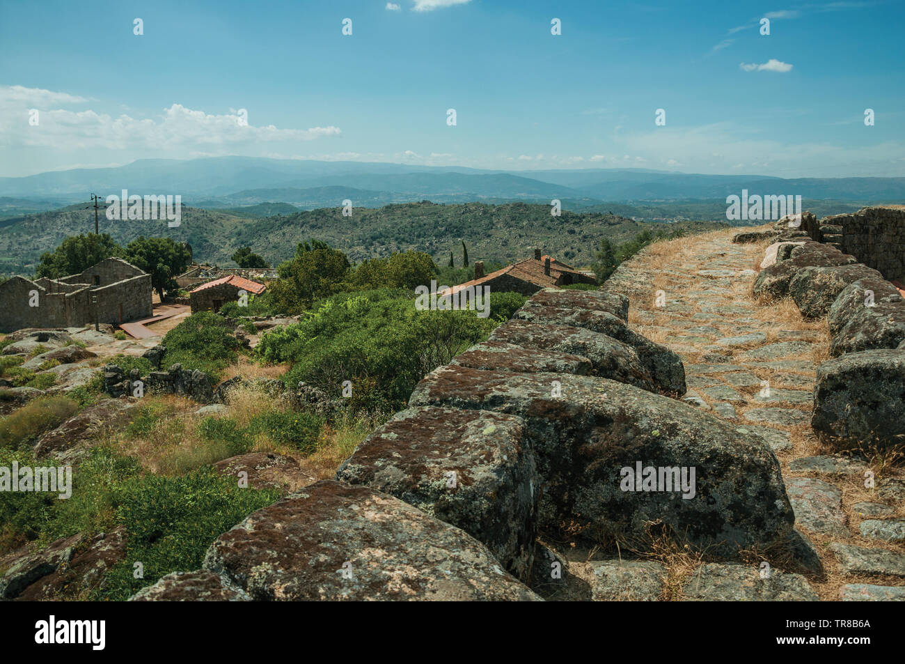 Pathway over stone wall next to old houses roofs and hilly landscape at ...