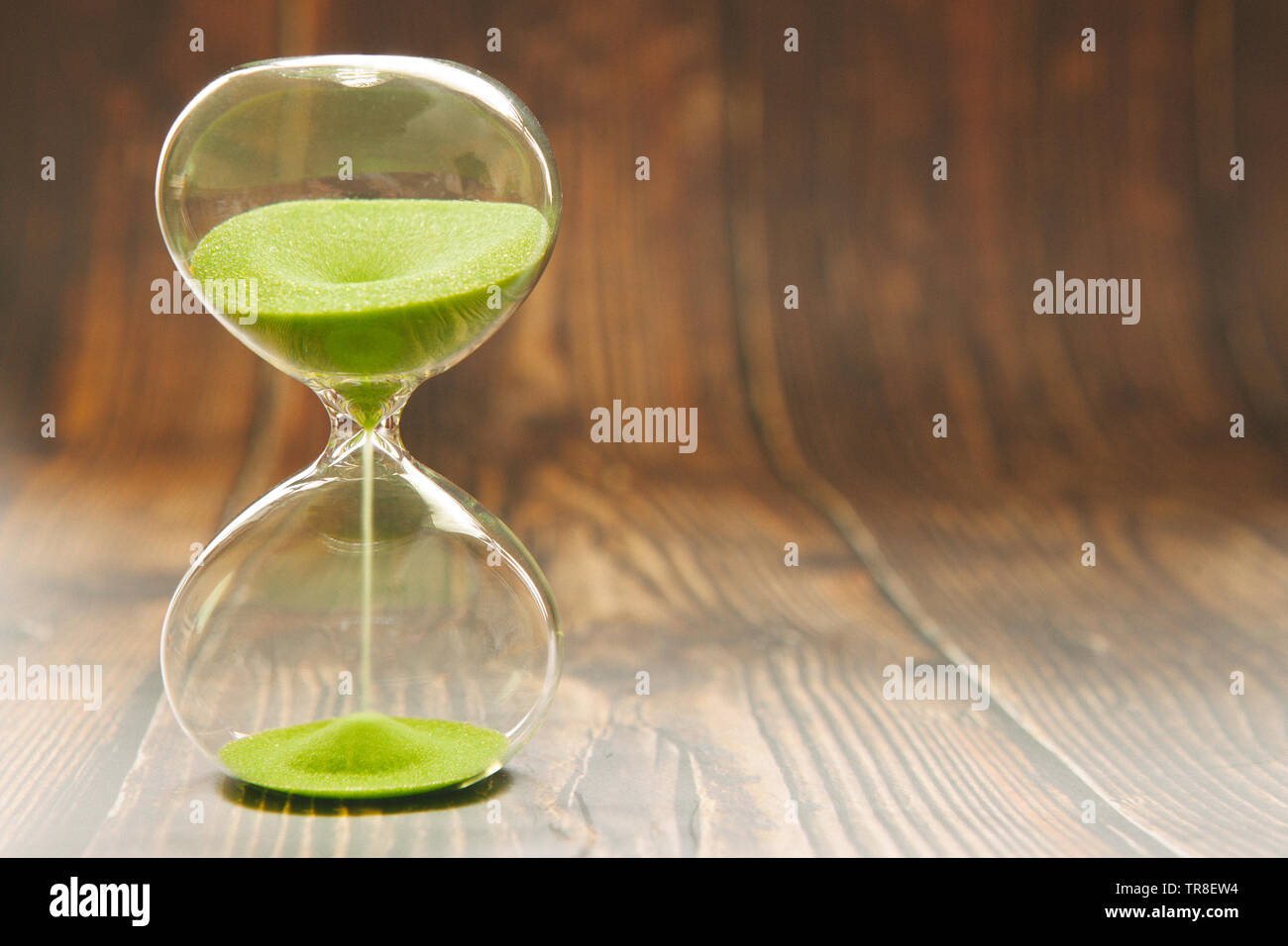 Hourglass with falling sand inside a glass bulb on a wooden daylight ...