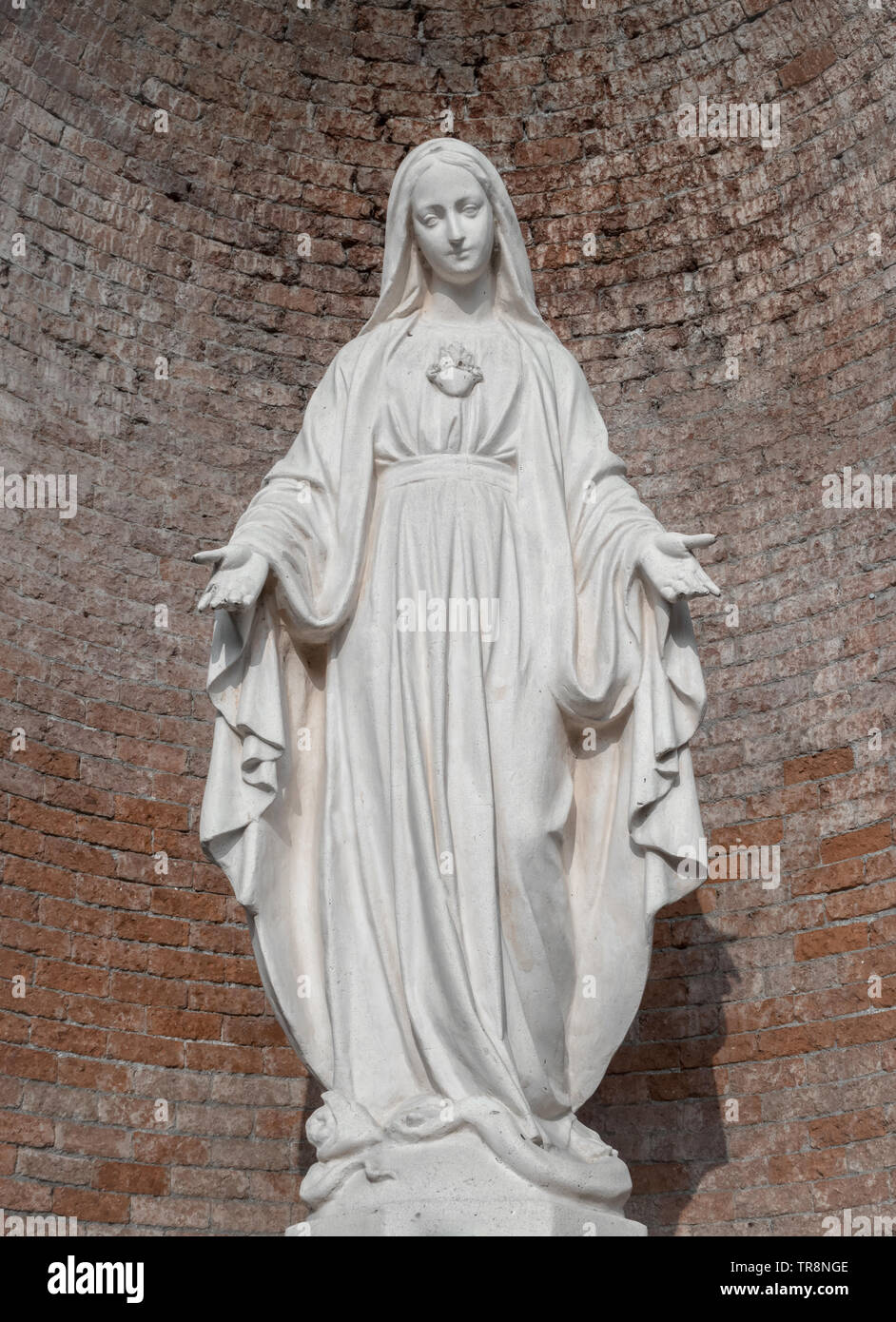 Statue in stone of Virgin Mary. On background, red brick wall. Ideal ...