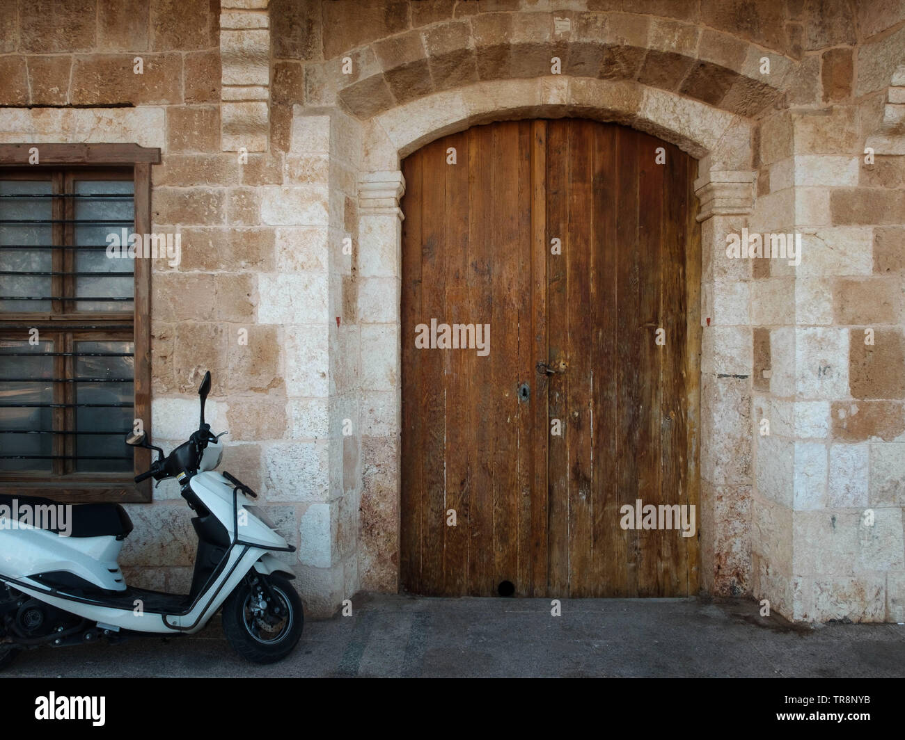 Parked scooter, wooden gates and barred window of antique stone ...