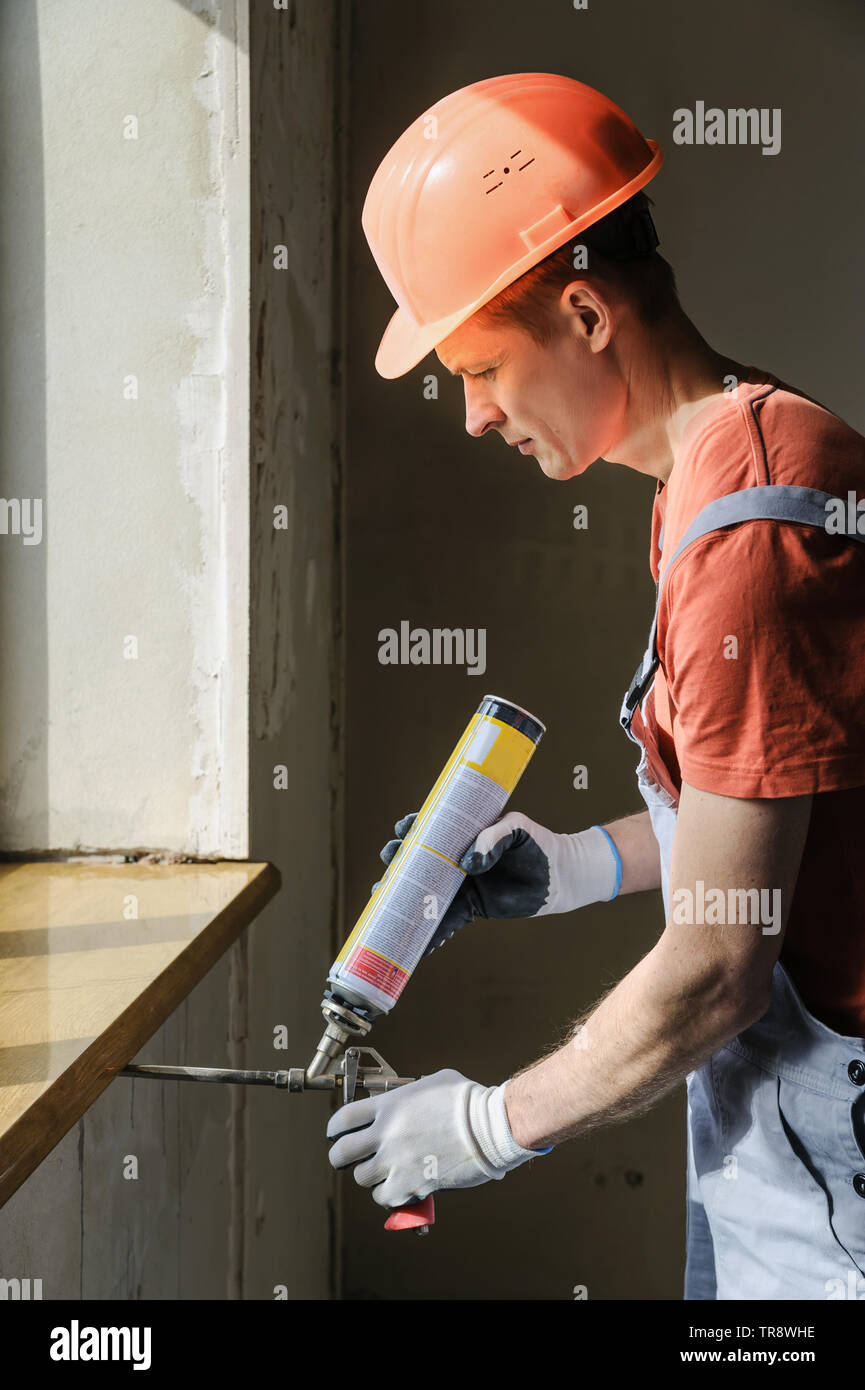 Worker is using a polyurethane foam for installation of window sill ...