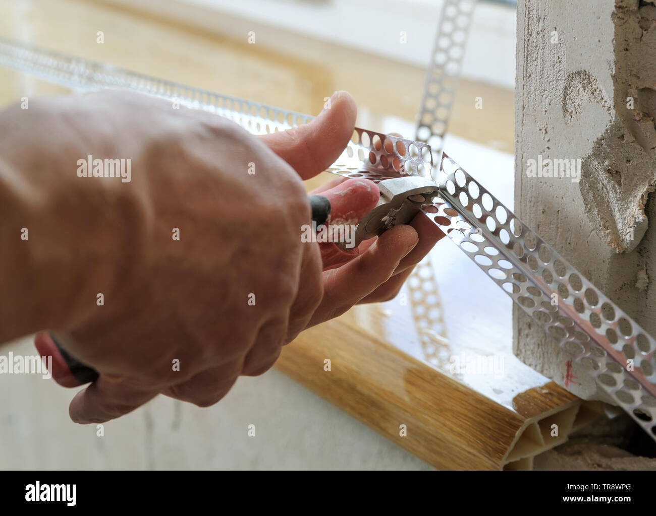 Worker's hands are cutting a perforated aluminum corner for ...