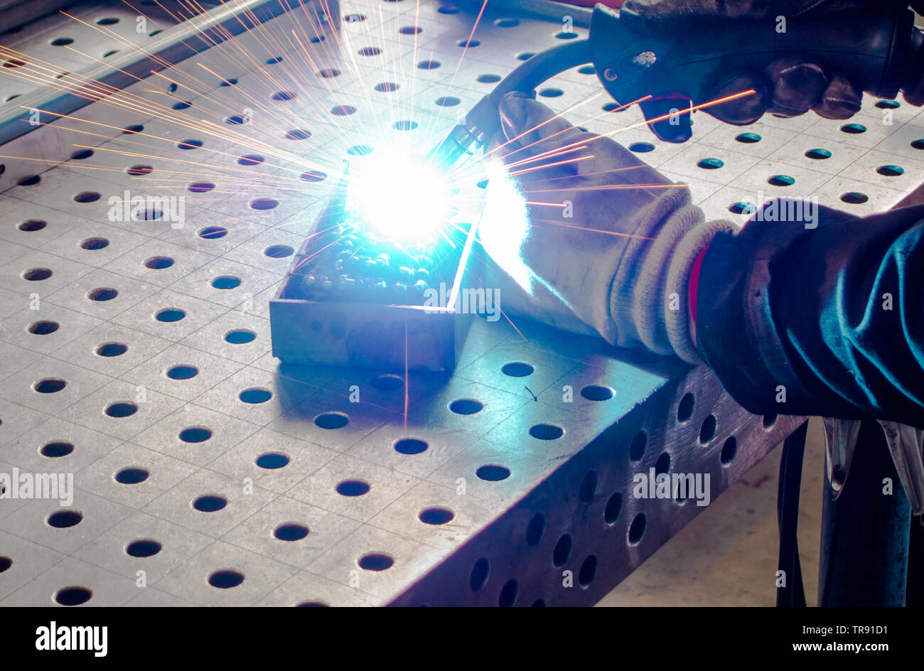 Worker with protective gloves welding steel on a welding table. Arc ...