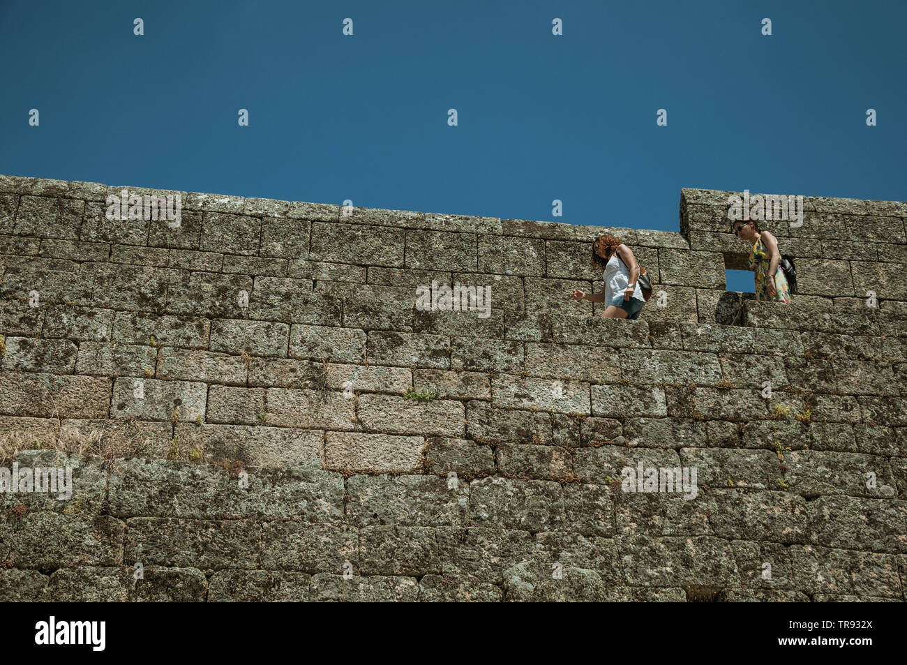 Women passing through a pathway over large stone wall at the Sortelha ...