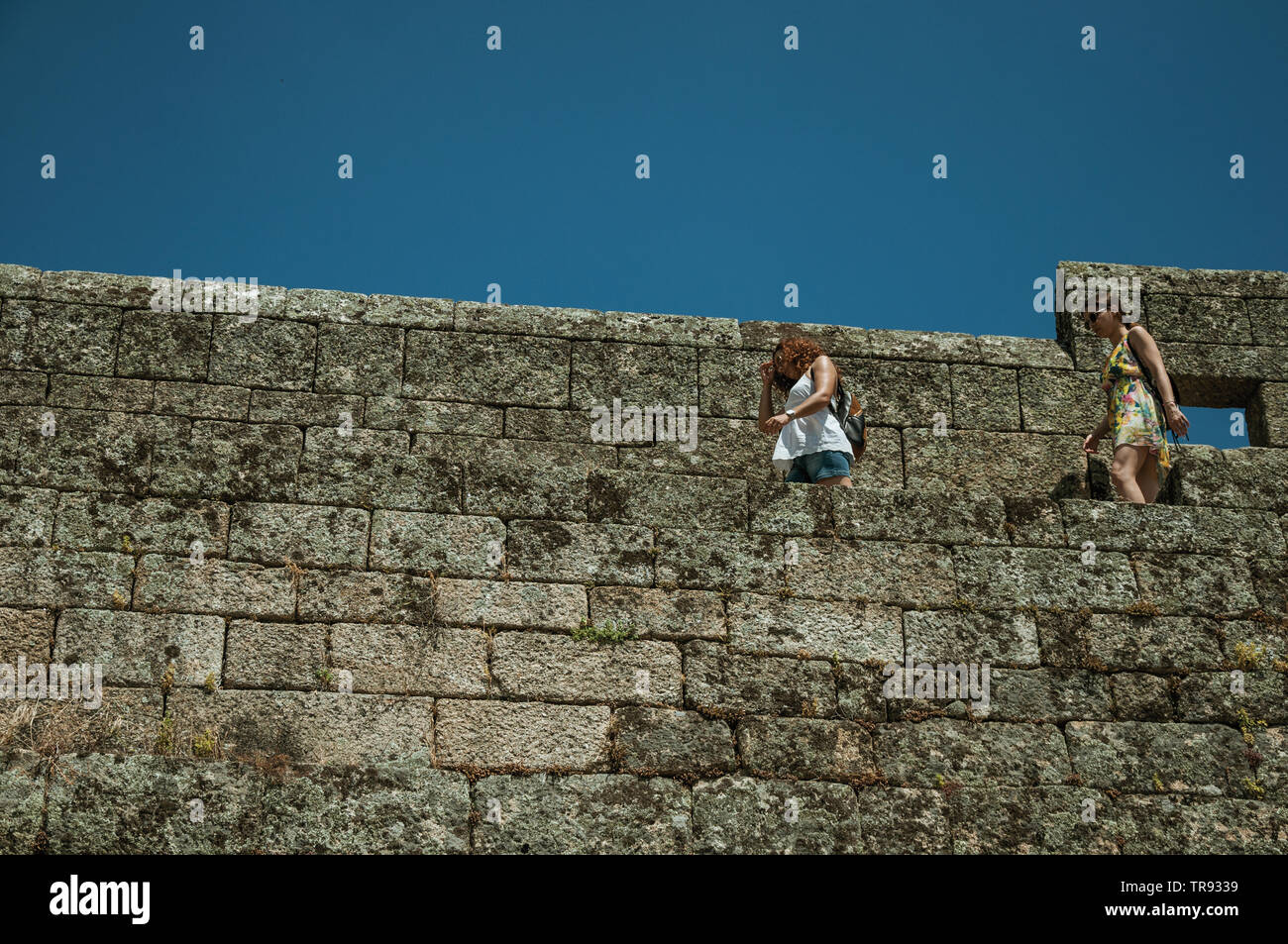 Women passing through a pathway over large stone wall at the Sortelha ...