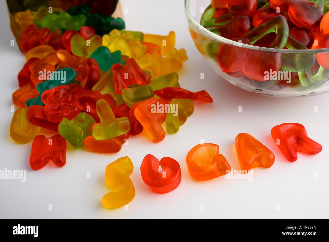 Glass bowls and paper bag of colorful gummy candies on white background ...