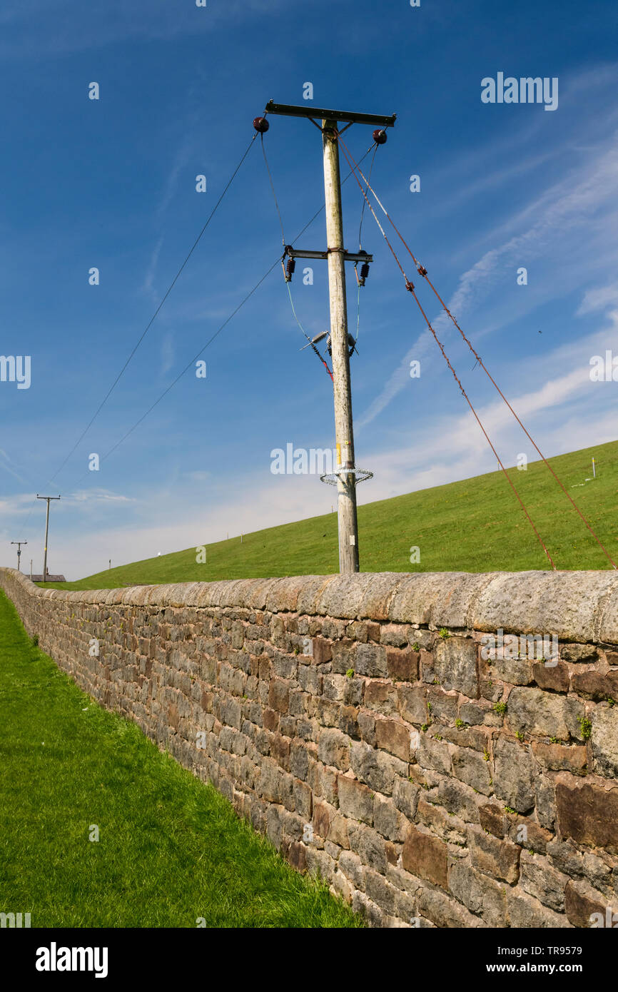 Stone wall, power line pole and danger sign against a blue sky Stock ...