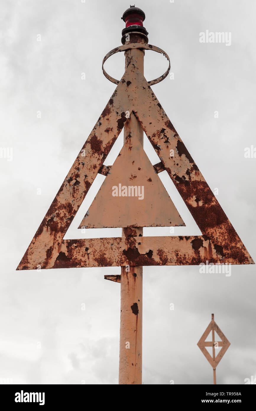 Rusty triangular navigation mark on metal pole under gray cloudy sky ...