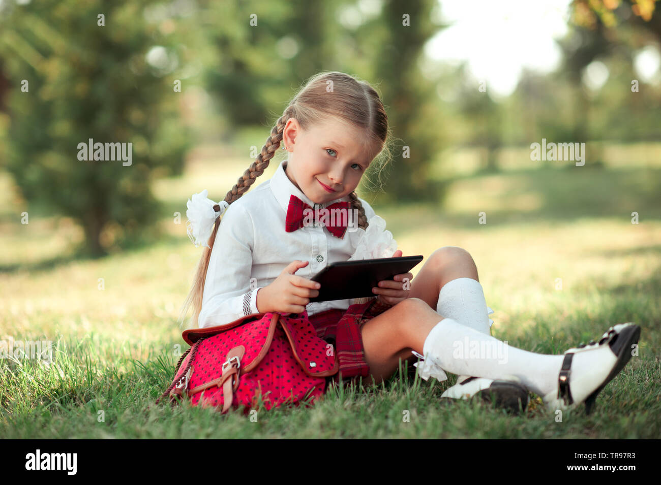 Funny kid girl 6-8 year old holding tablet outdoors. Looking at camera ...