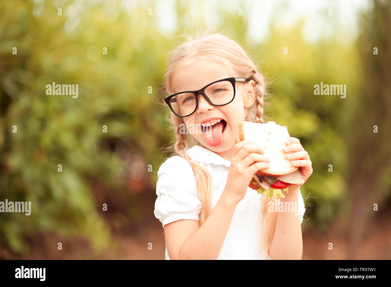 Funny kid girl eating sandwich outdoors. Having fun. Looking at camera ...