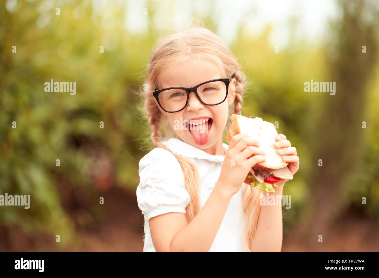 Funny kid girl eating sandwich outdoors. Having fun. Looking at camera ...