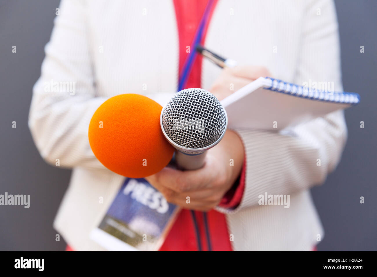Female journalist at news conference, writing notes, holding microphone ...