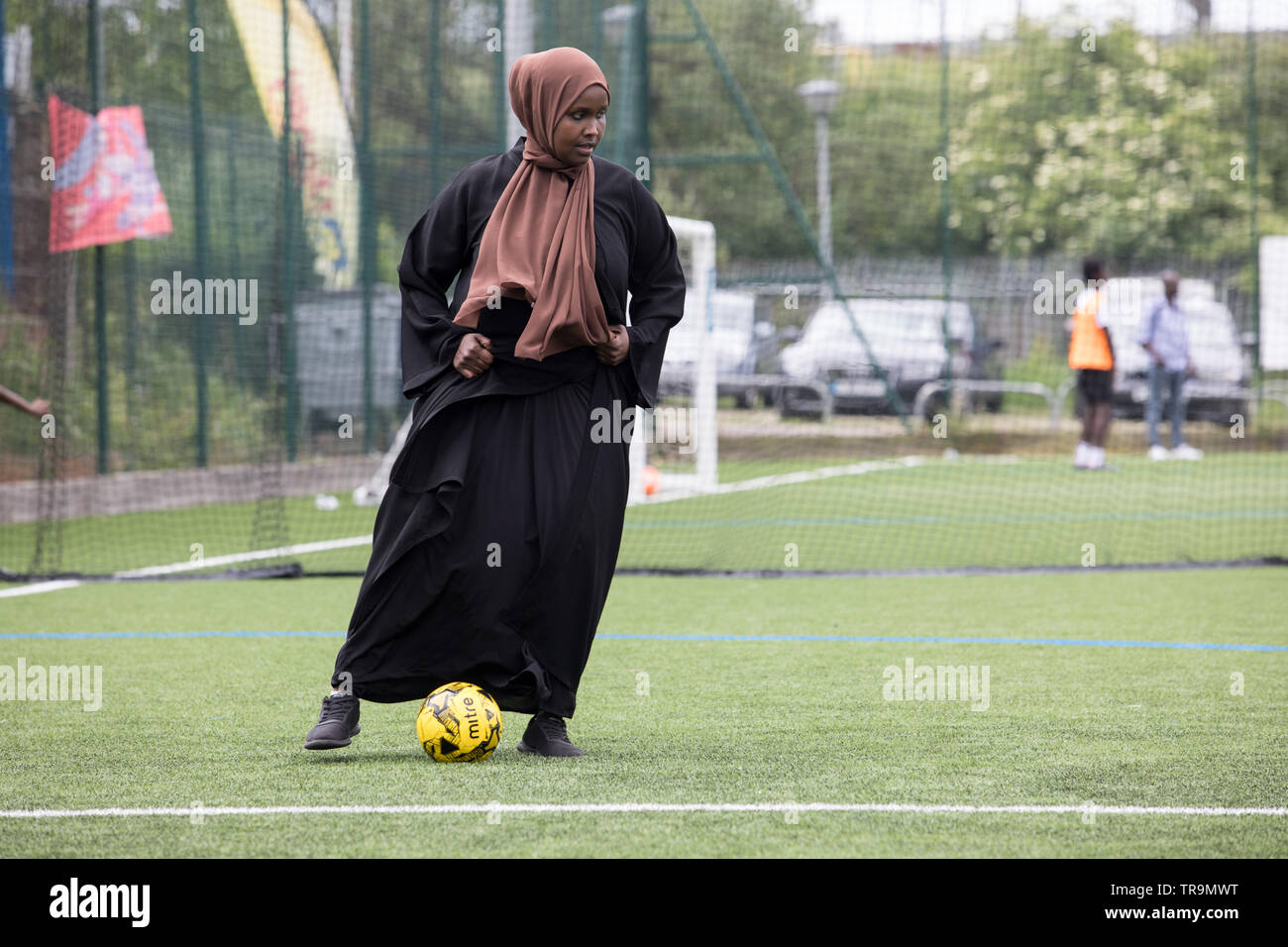 A Muslim woman dribbles a football on an astroturf pitch, dressed ...
