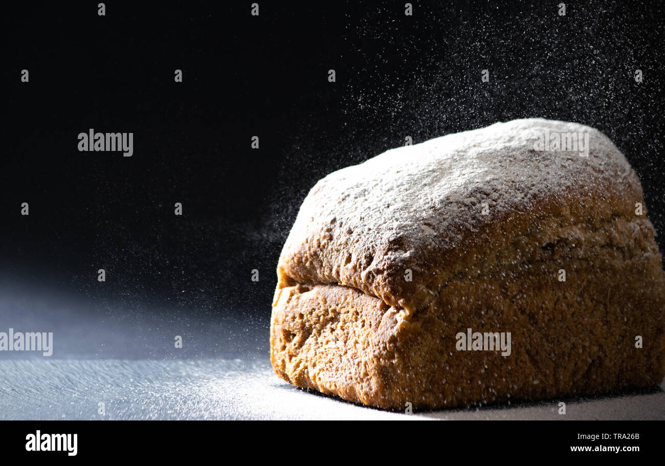 Close up bread with falling flour on black background. Bread making ...