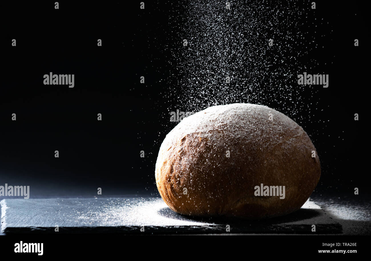 Close up bread with falling flour on black background. Bread making ...