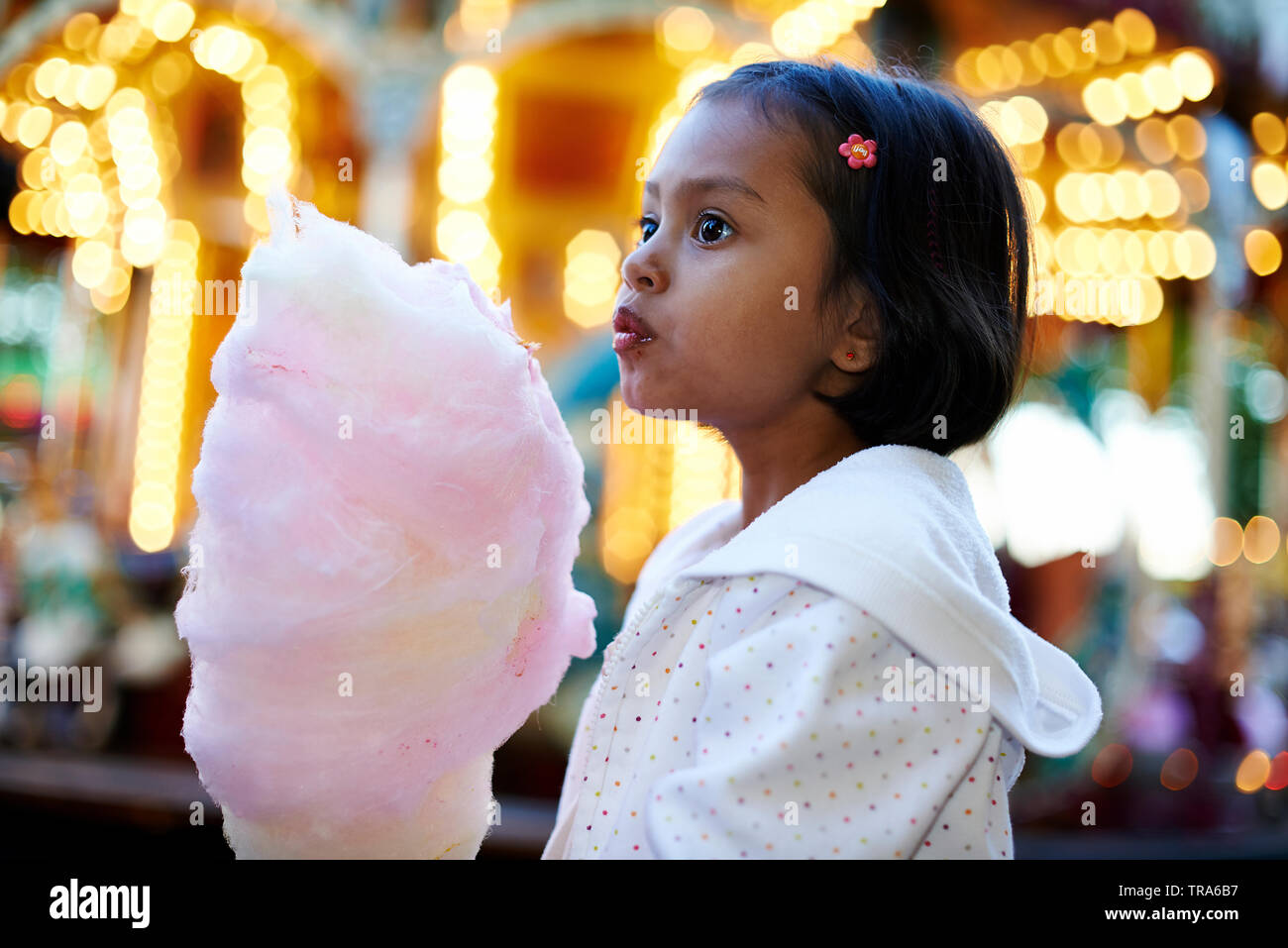 A young Asian girl enjoying a rather large piece of candy floss whilst ...