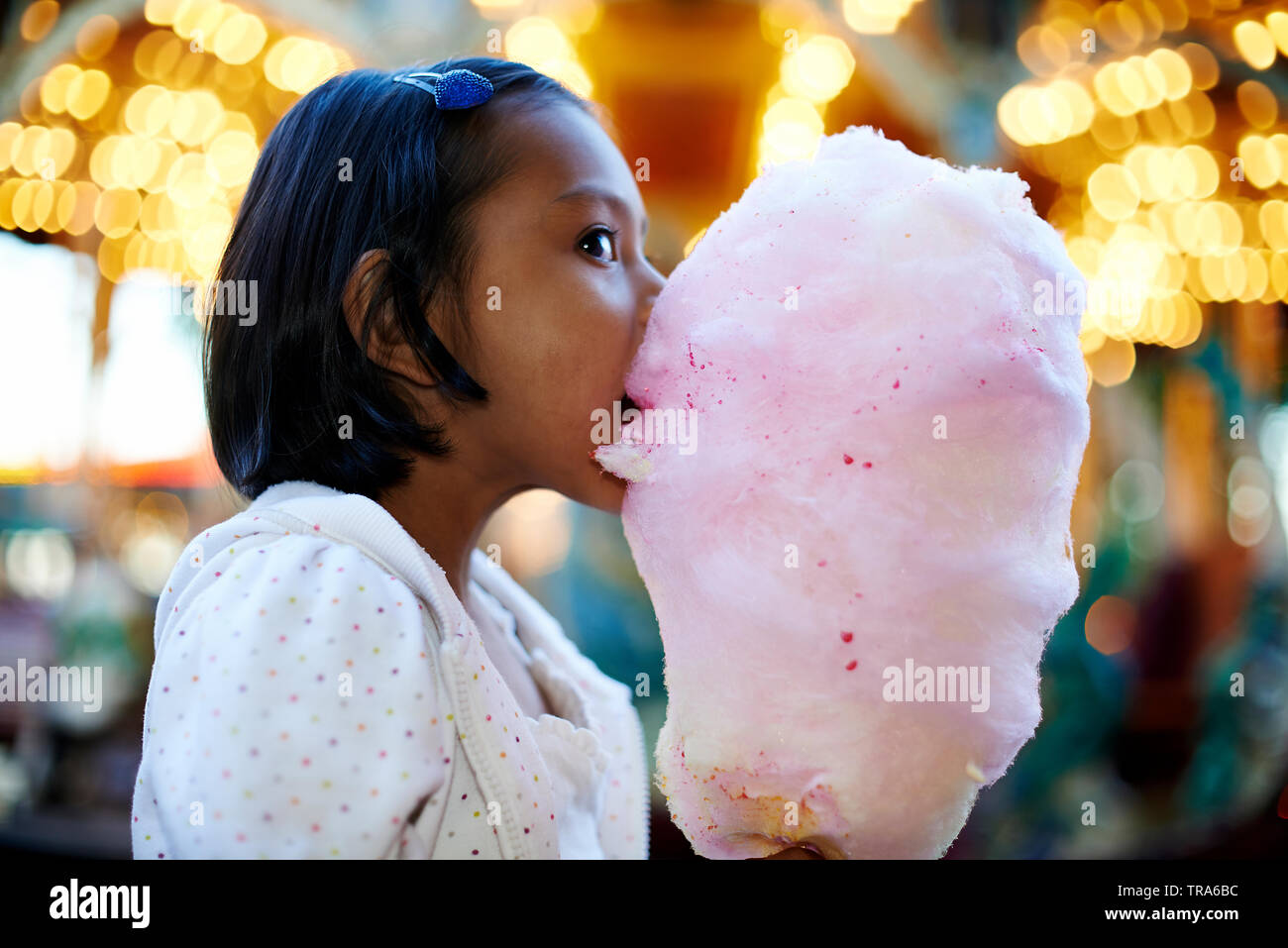 A young Asian girl enjoying a rather large piece of candy floss whilst ...