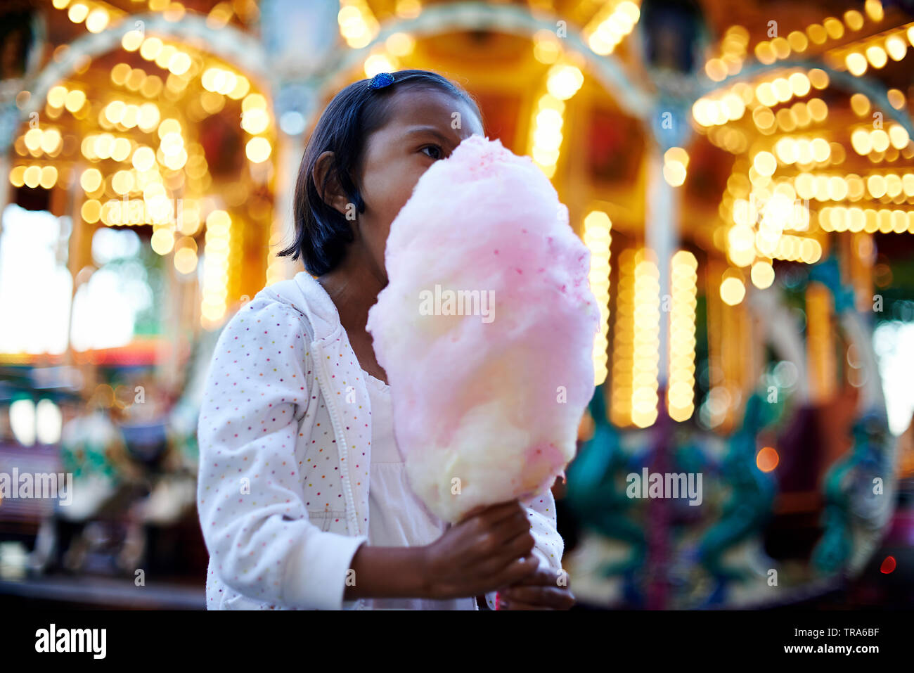 A young Asian girl enjoying a rather large piece of candy floss whilst ...