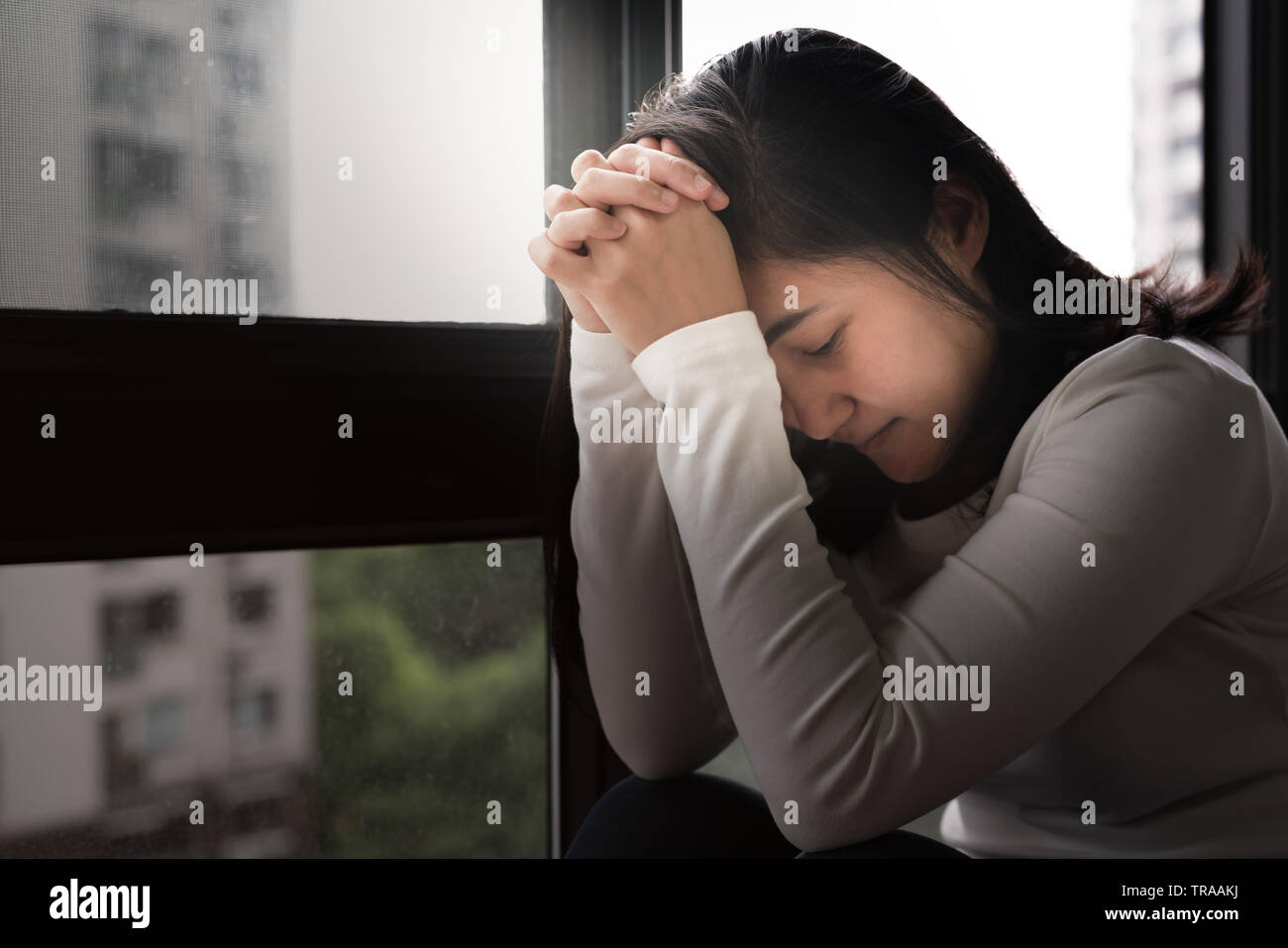 depressed women sitting near window and praying, alone, sadness ...