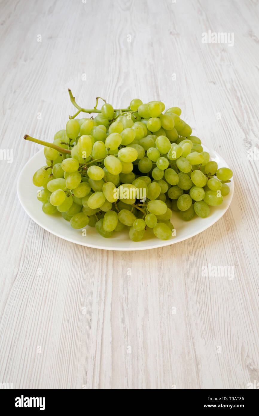 Green grape on a white plate over white wooden background, side view ...
