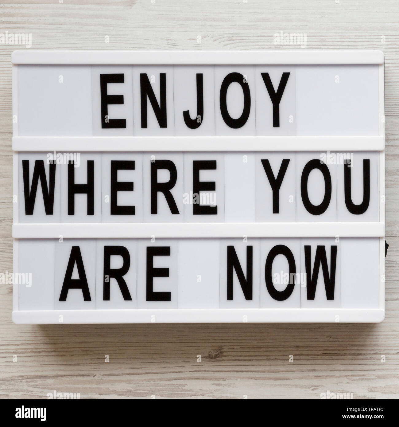 'Enjoy where you are now' words on a modern board over white wooden ...