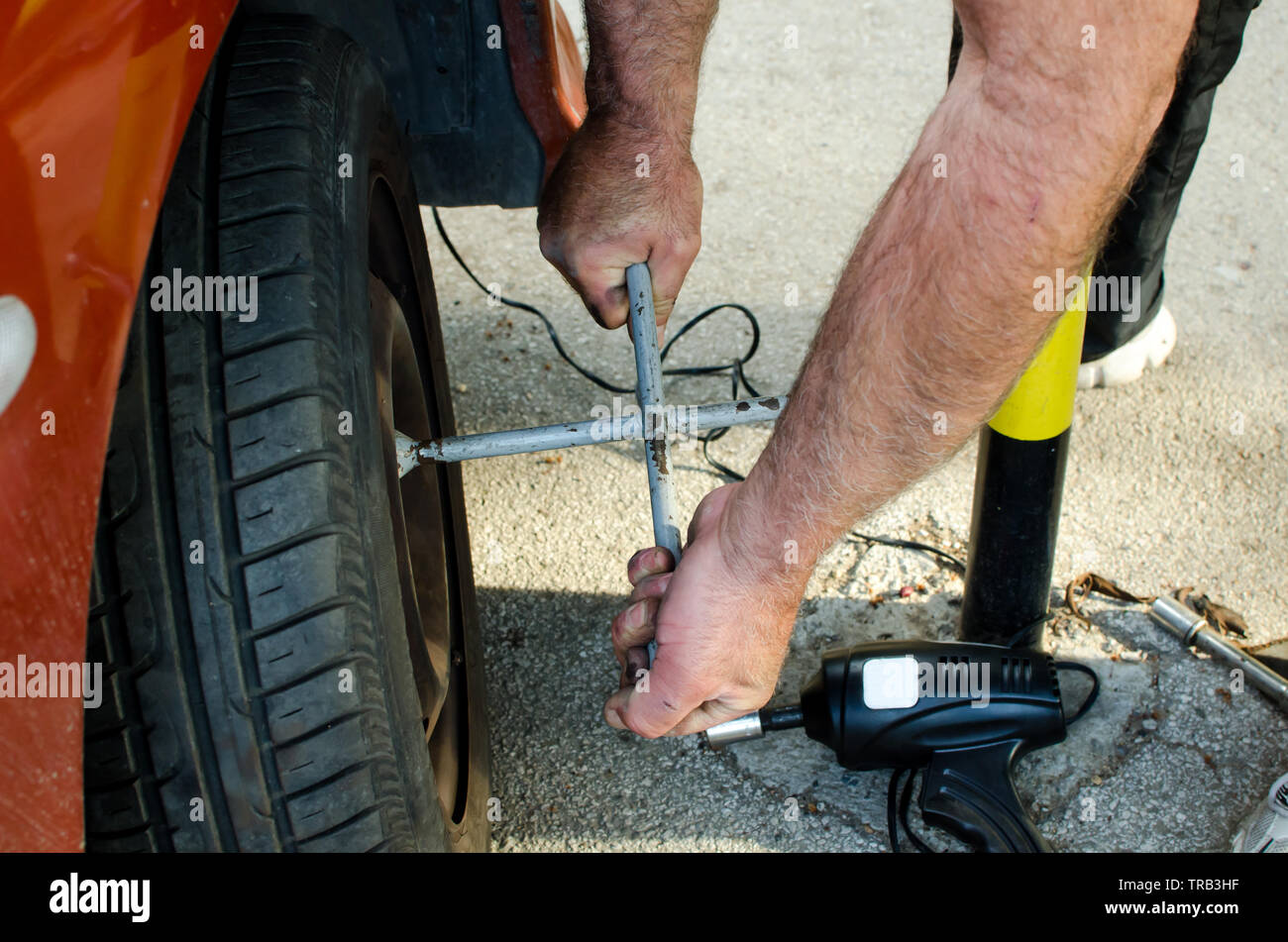 side view of mechanic changing wheel on car with a wrench on street ...