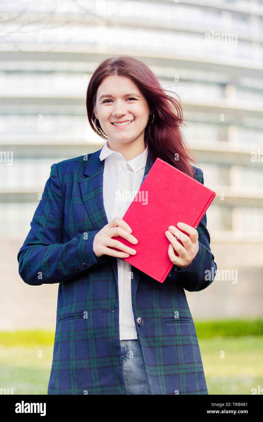 Smiling Student girl outdoors holding a books book over bulding ...