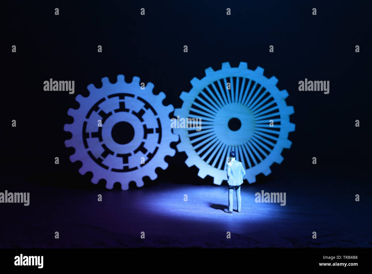 Miniature man looking at cogwheel in set of gears mechanism. Problem ...
