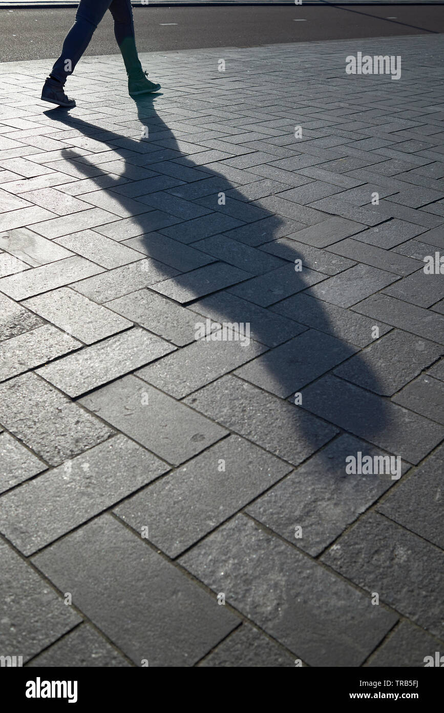 Low angle of the legs and shadows of people walking past in bright ...