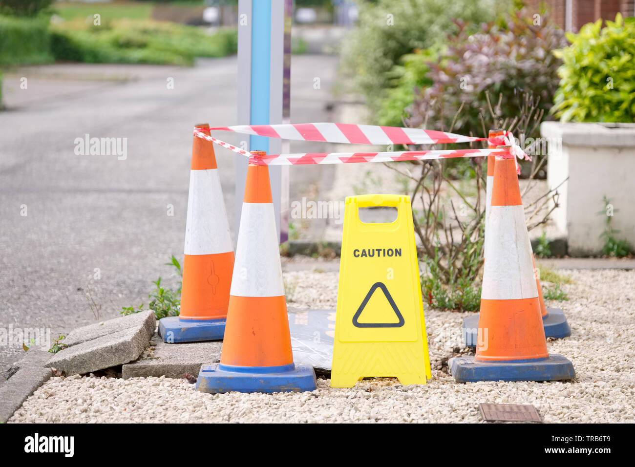 Caution yellow sign and orange traffic cones protecting excavation hole ...