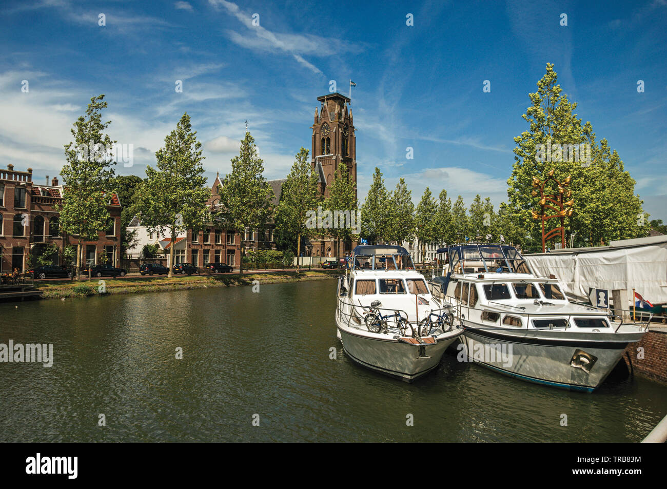 Boats moored on the canal margin, trees and brick buildings under a ...