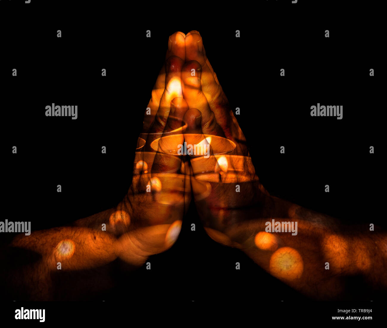 Praying hands over burning candles Stock Photo - Alamy