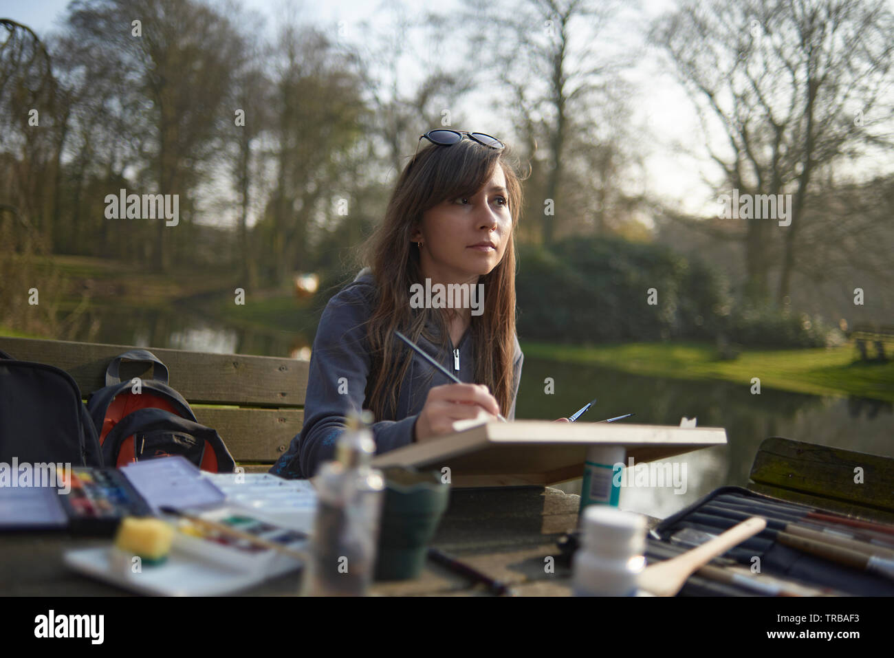 Young creative female artist sitting on a bench in a park painting a ... Young creative female artist sitting on a bench in a park painting a ...