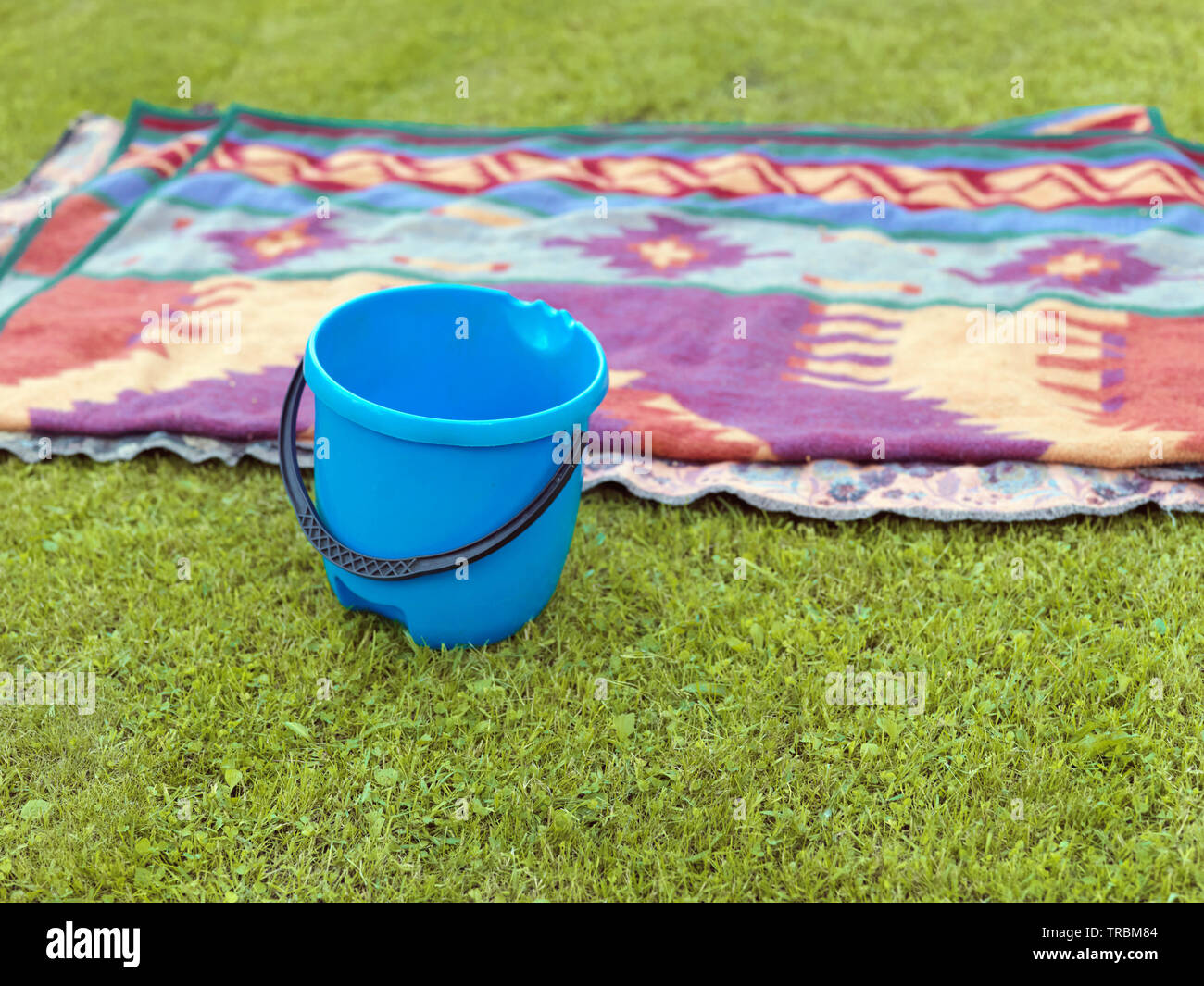 A plastic bucket next to the colorful carpet needs cleaning, outdoor ...