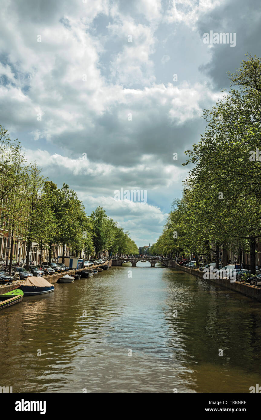 Tree-lined canal with old brick buildings, bridge and moored boats in ...