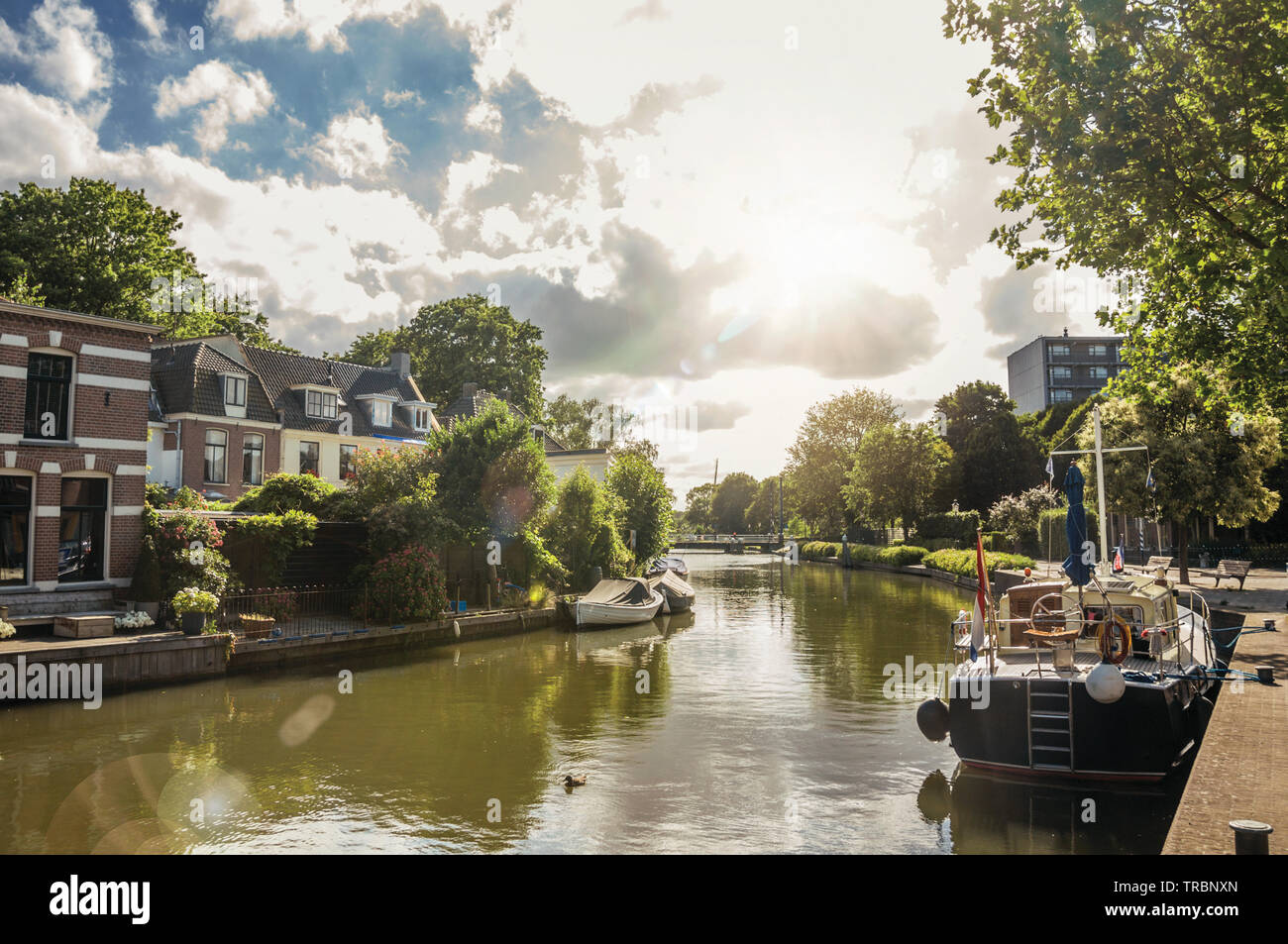 Wide canal with cloudy sky, houses and boat moored reflected in water ...