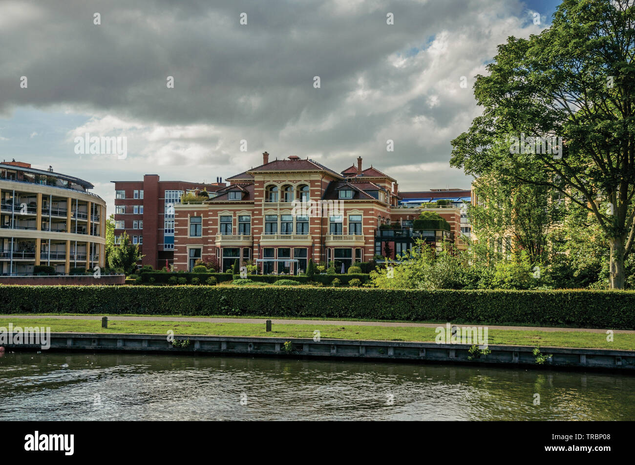 Fancy brick building next to wide tree-lined canal under cloudy sky in ...