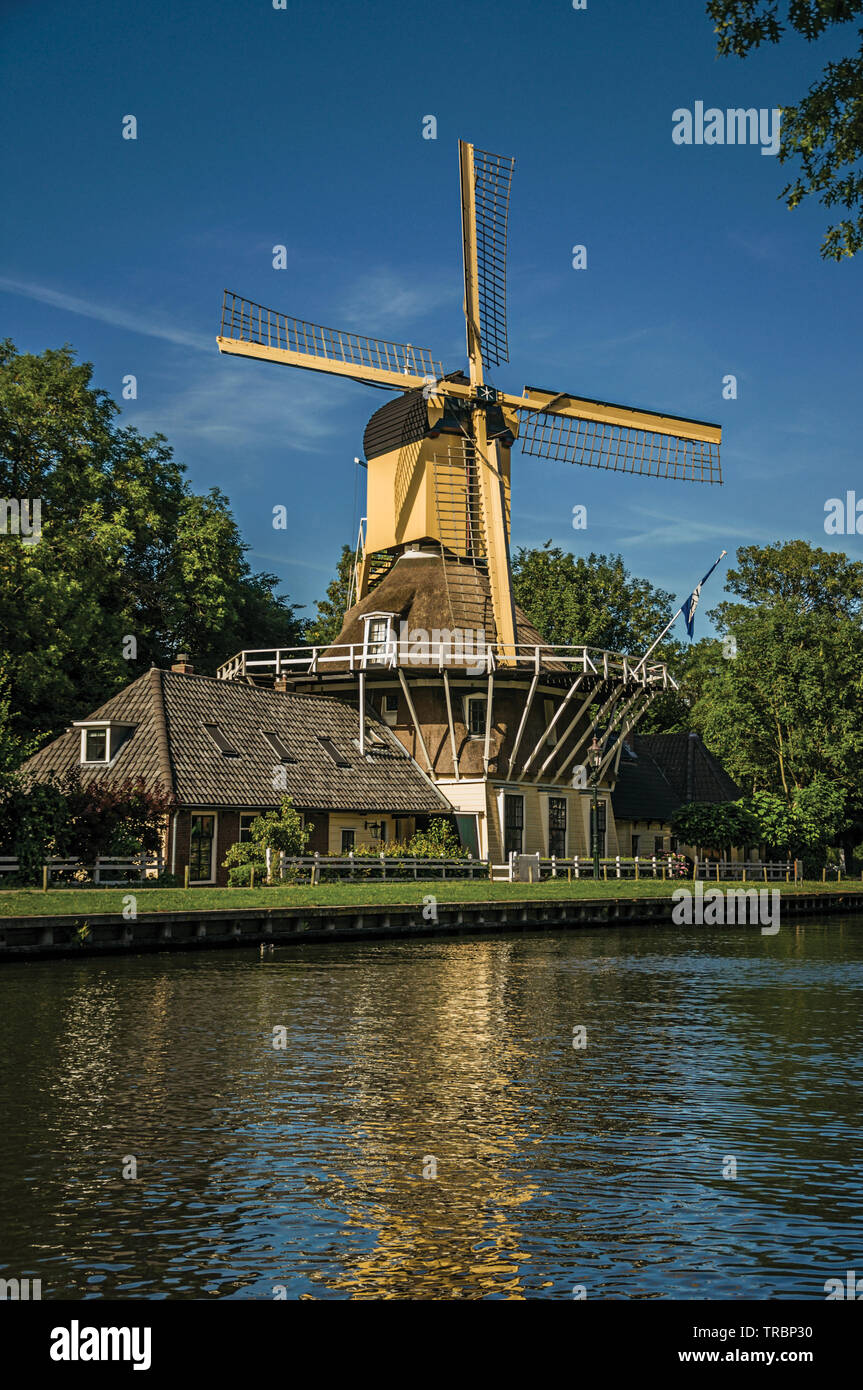 House and wooden yellow windmill next to wide tree-lined canal on ...